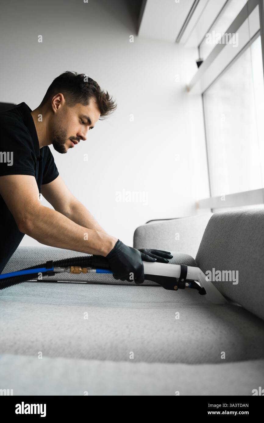 Cleaner is dry-cleaning sofa using extractor machine with detergent ...