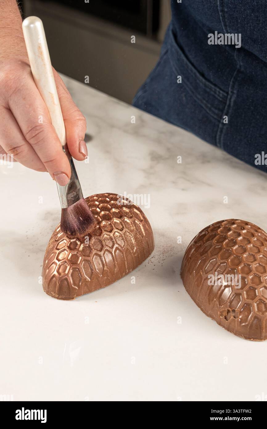 Confectioner putting edible copper powder on a chocolate Easter egg ...