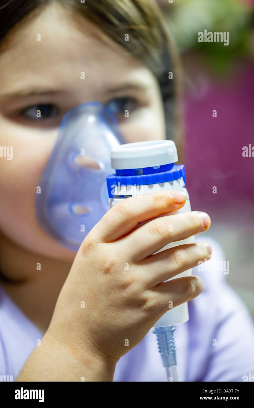 Child using nebulizer for respiratory treatment at home while feeling ...