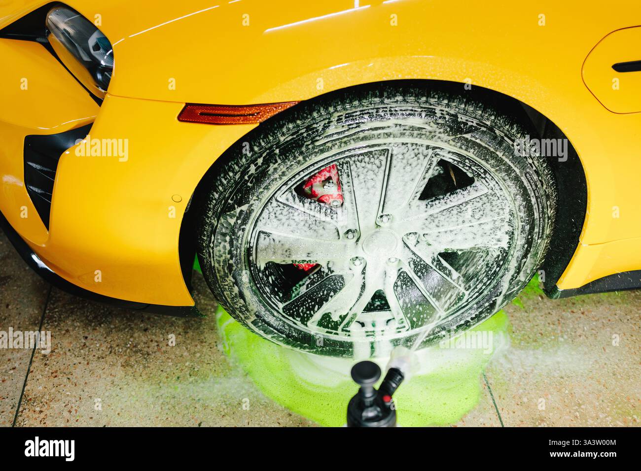 Spraying detergent on tire of a yellow sports car using a spray with ...