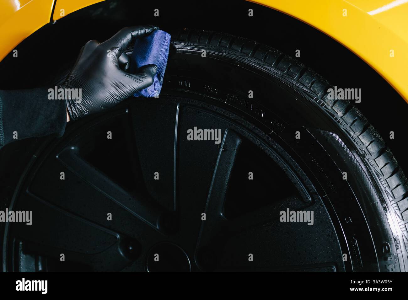 Mechanic applies a product to a black tire using a blue applicator ...