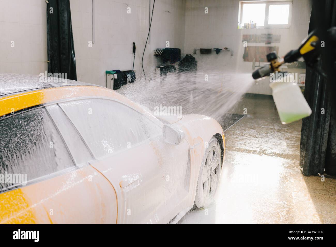 High-pressure water gun spraying soapy solution onto the vehicle's ...