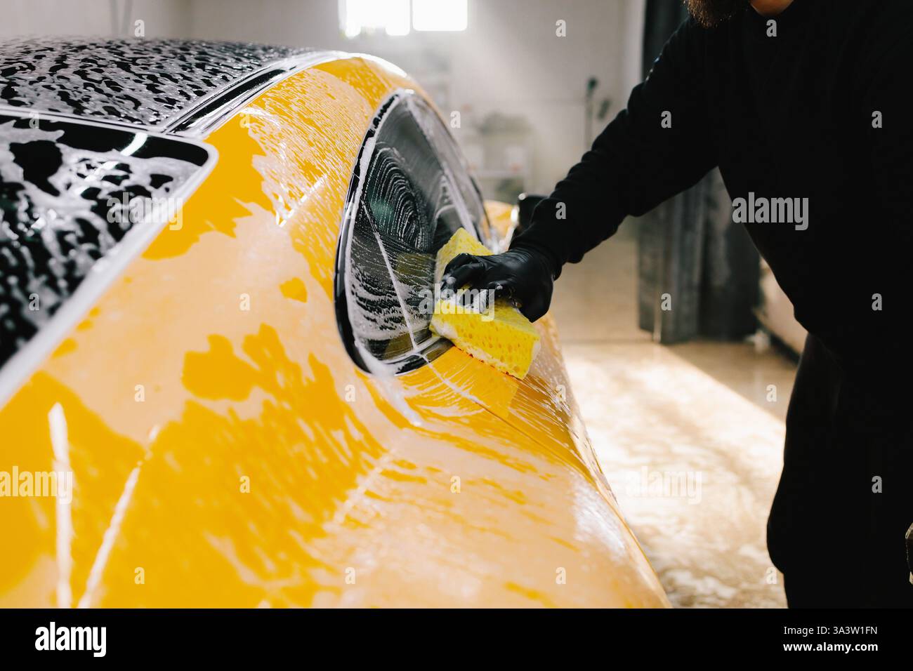 Hand washing with yellow sponge and foam for sports car body in garage ...
