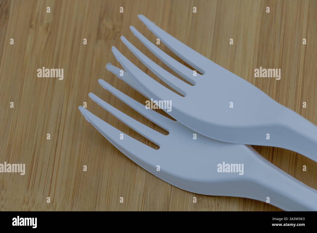 Two white plastic fork pieces stacked on top of each other on a bamboo ...