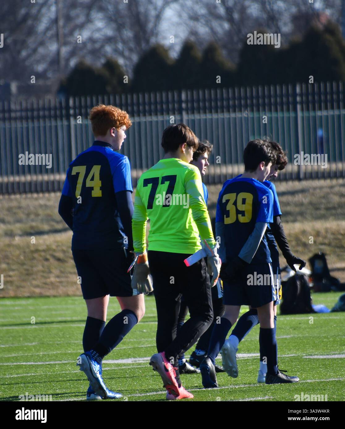 Teammates walk off the pitch following a soccer match, wearing blue and ...