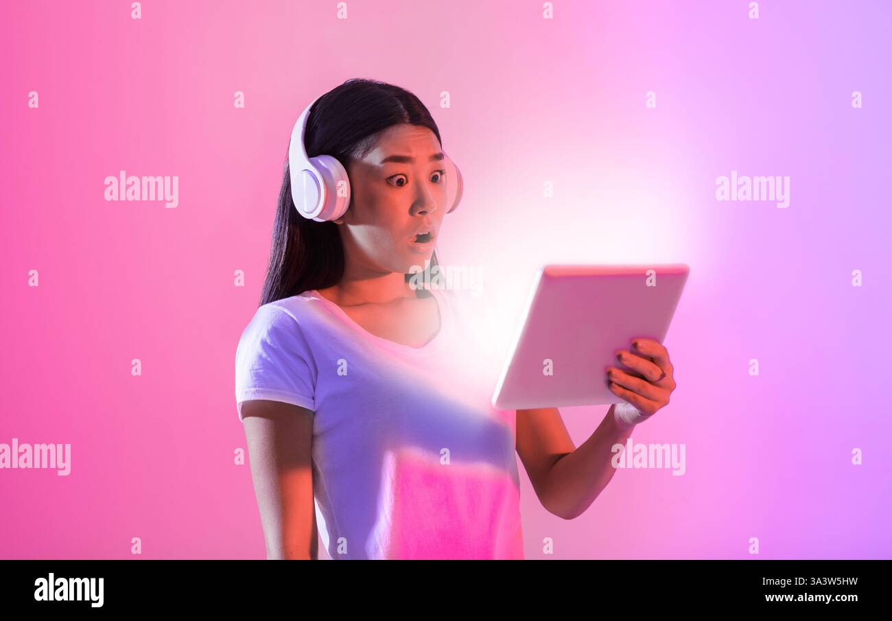 Young woman reacts with surprise while using a tablet in colorful ...