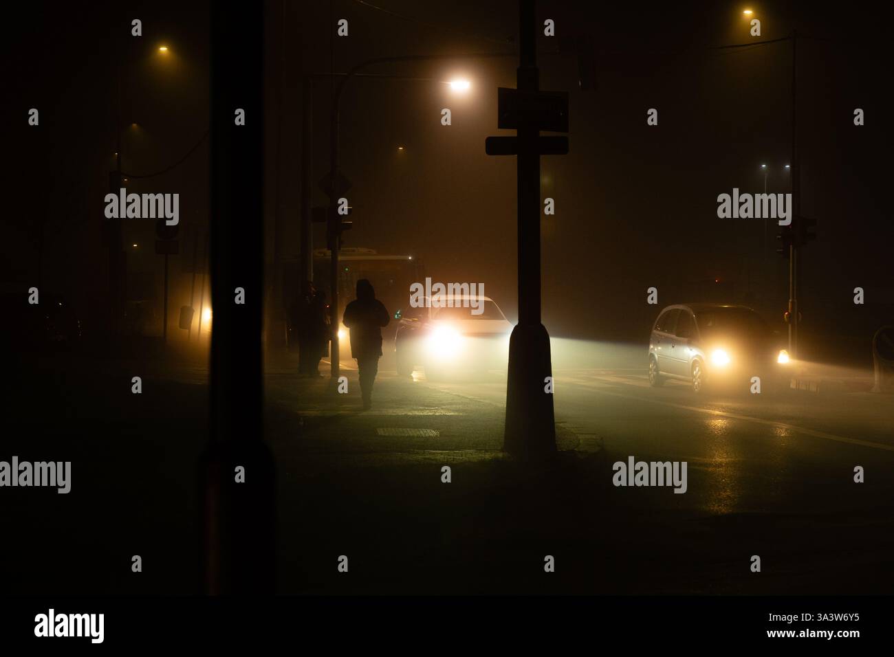 Night intersection with cars, bus and pedestrians illuminated by orange ...
