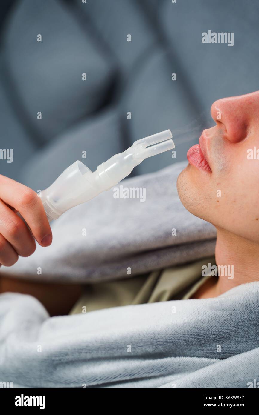 Doing nose inhalation with nebulizer at home. Young man with asthma ...
