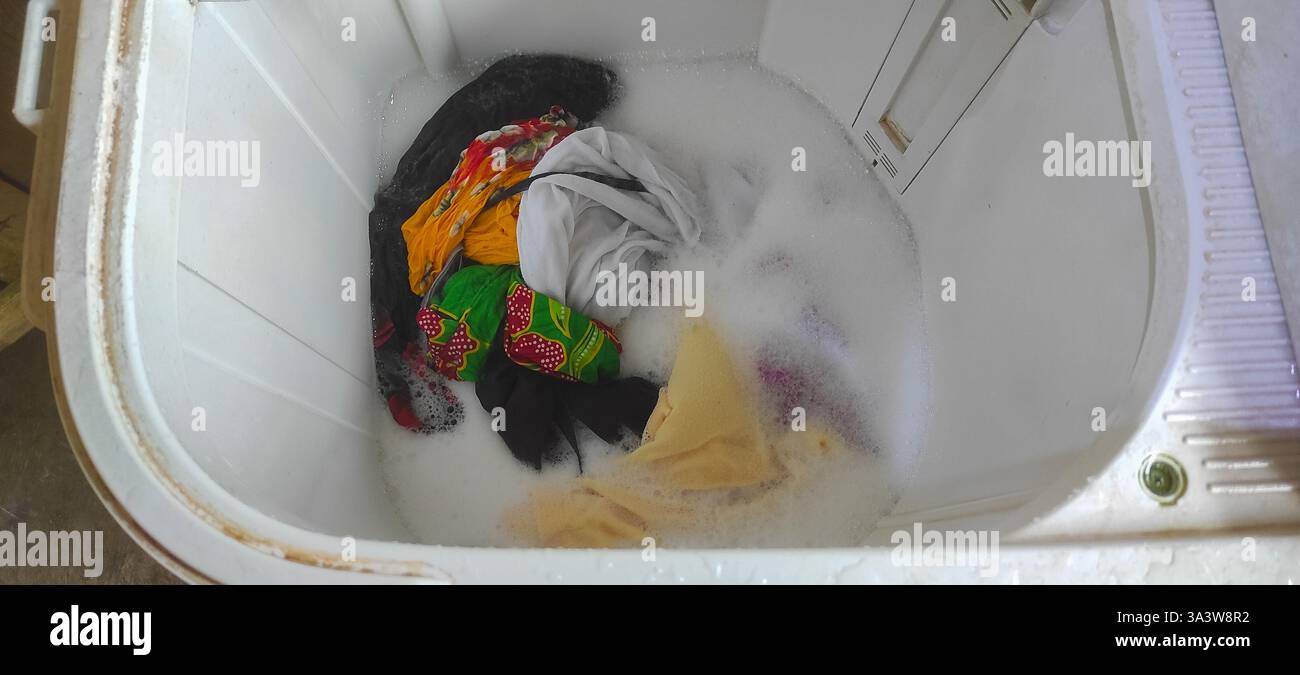 old, dirty washing machine with clothes soaking in soapy water, showing ...