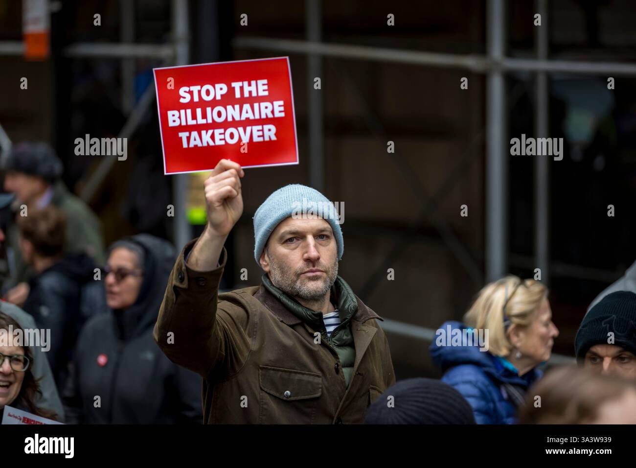 A protestor holds a sign that says "Stop the billionaire takeover" as ...