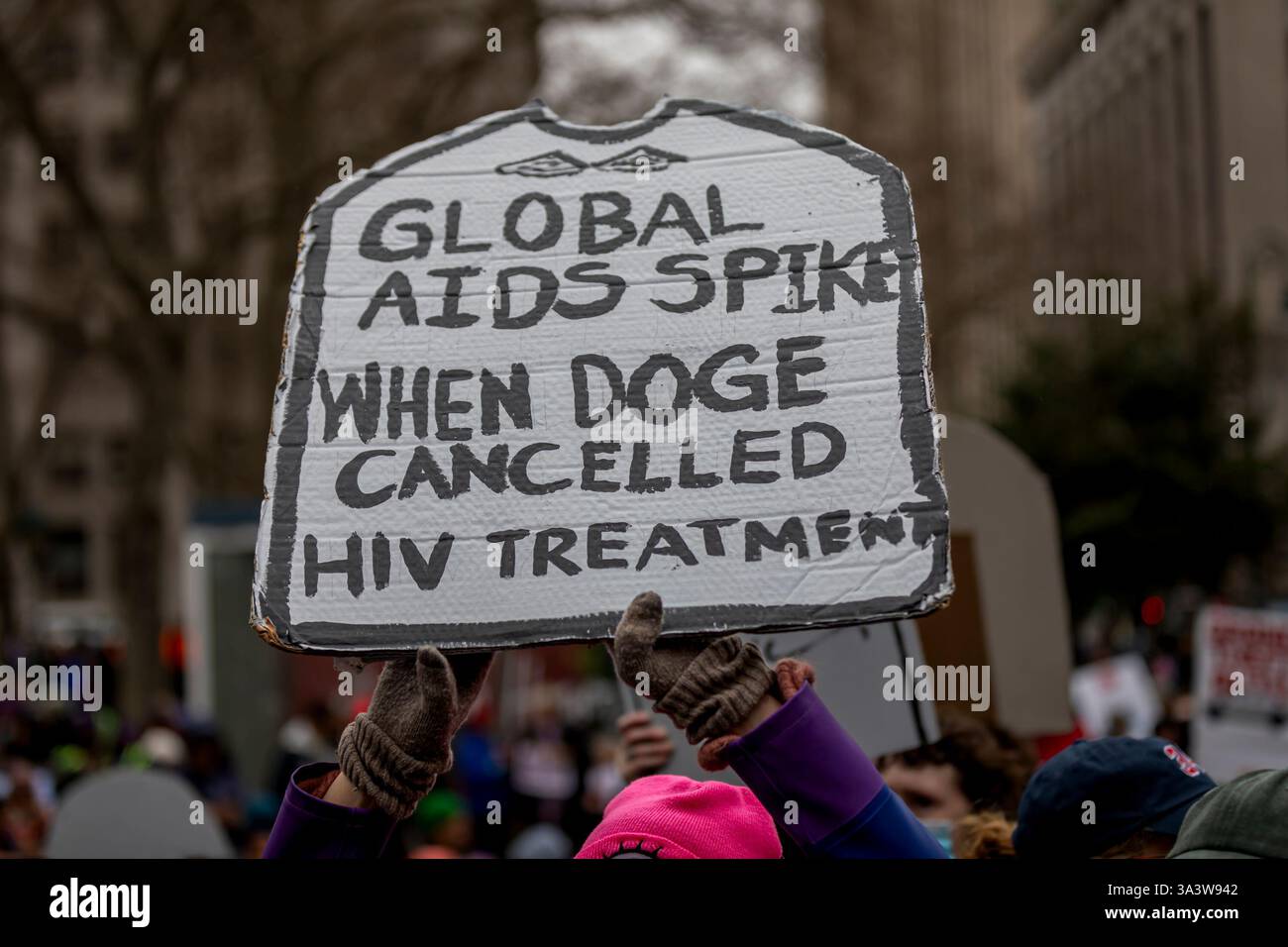 A protestor holds a sign that says "Global AIDS spike when DOGE ...