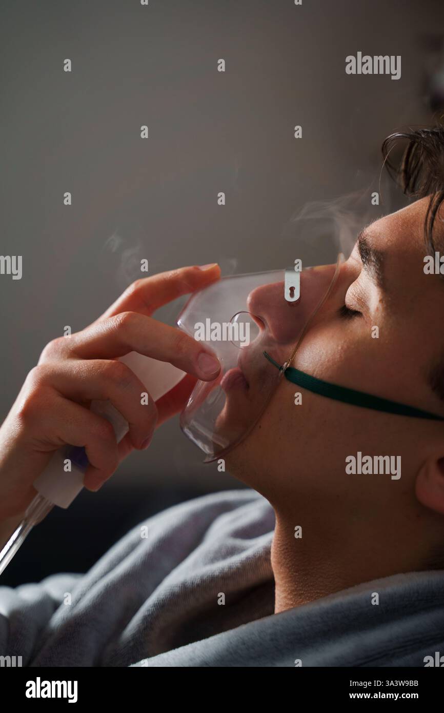 Man inhaling through oxygen mask for cough treatment. Using compressor ...
