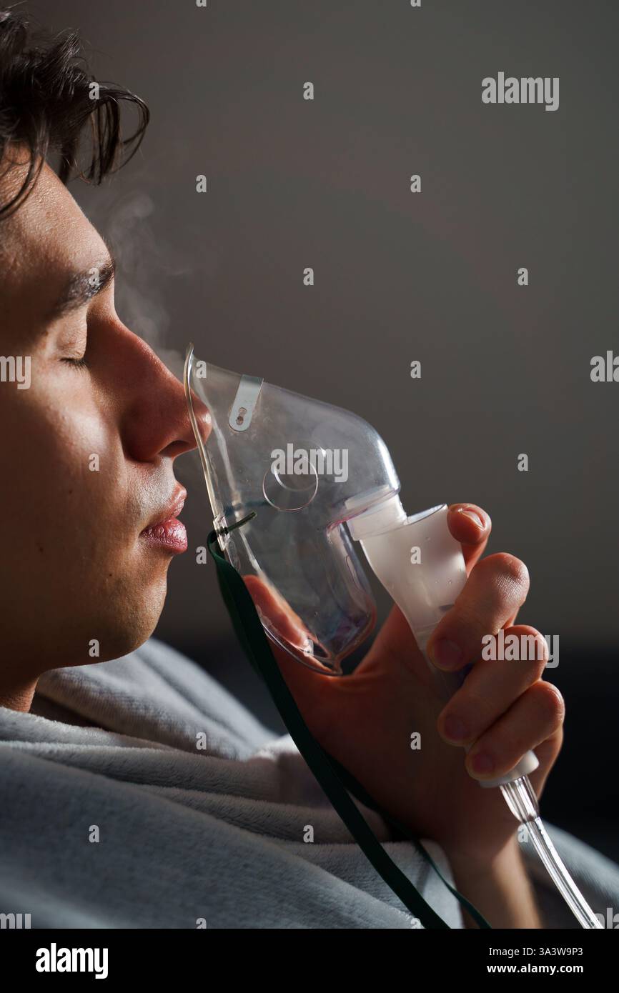 Man inhaling through oxygen mask for cough treatment. Using compressor ...