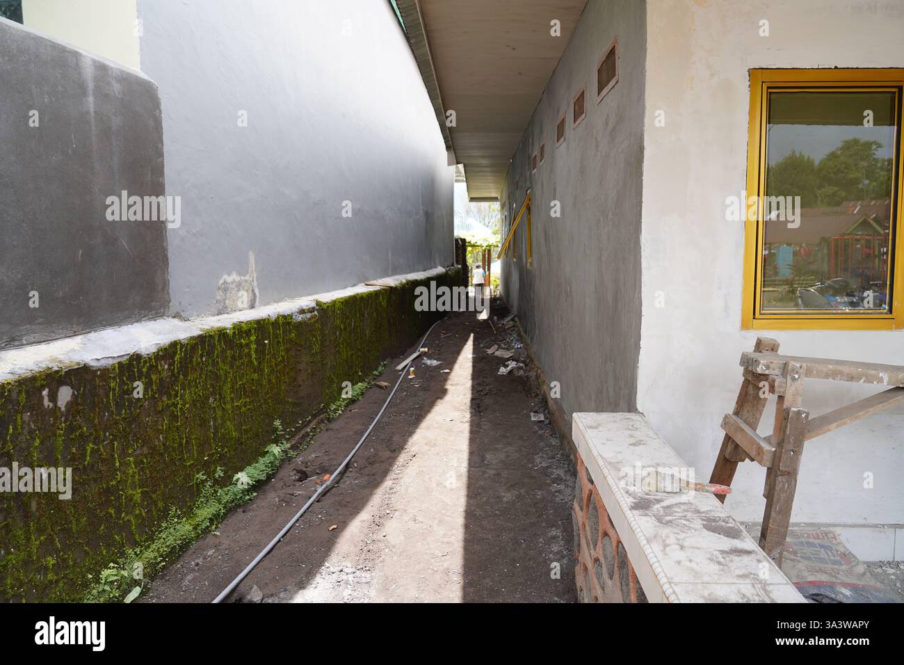 A narrow alley between two buildings with unfinished painted walls. One ...