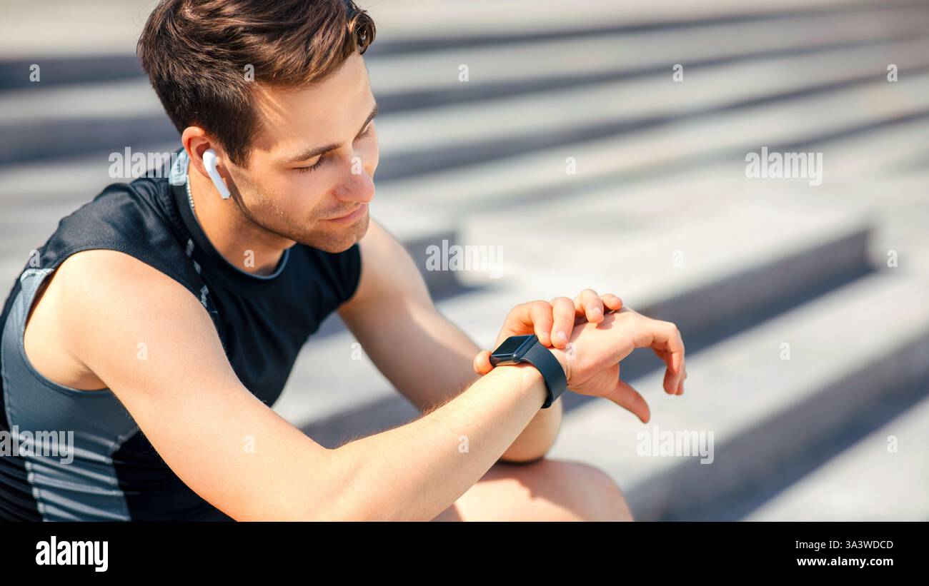 Modern jogging gadgets. Tired athlete with wireless headphones looks at ...