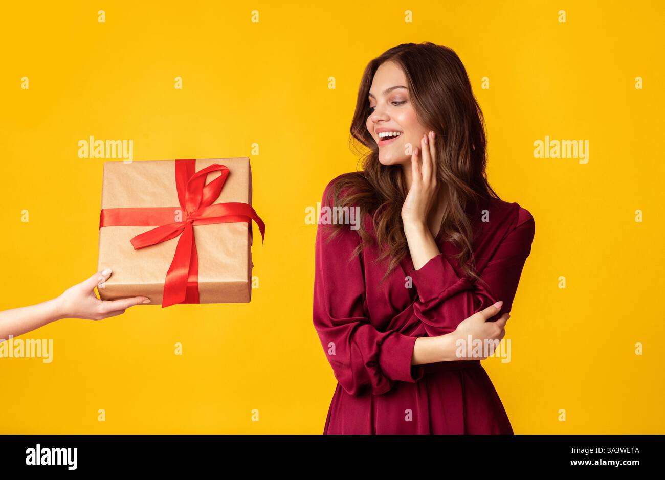 Surprised woman unwrapping a gift with a red ribbon on yellow Stock ...