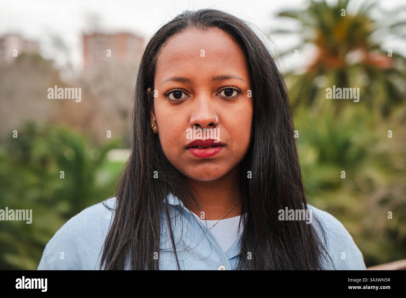A confident woman with striking long hair gazes directly at the camera with a serious expression ...