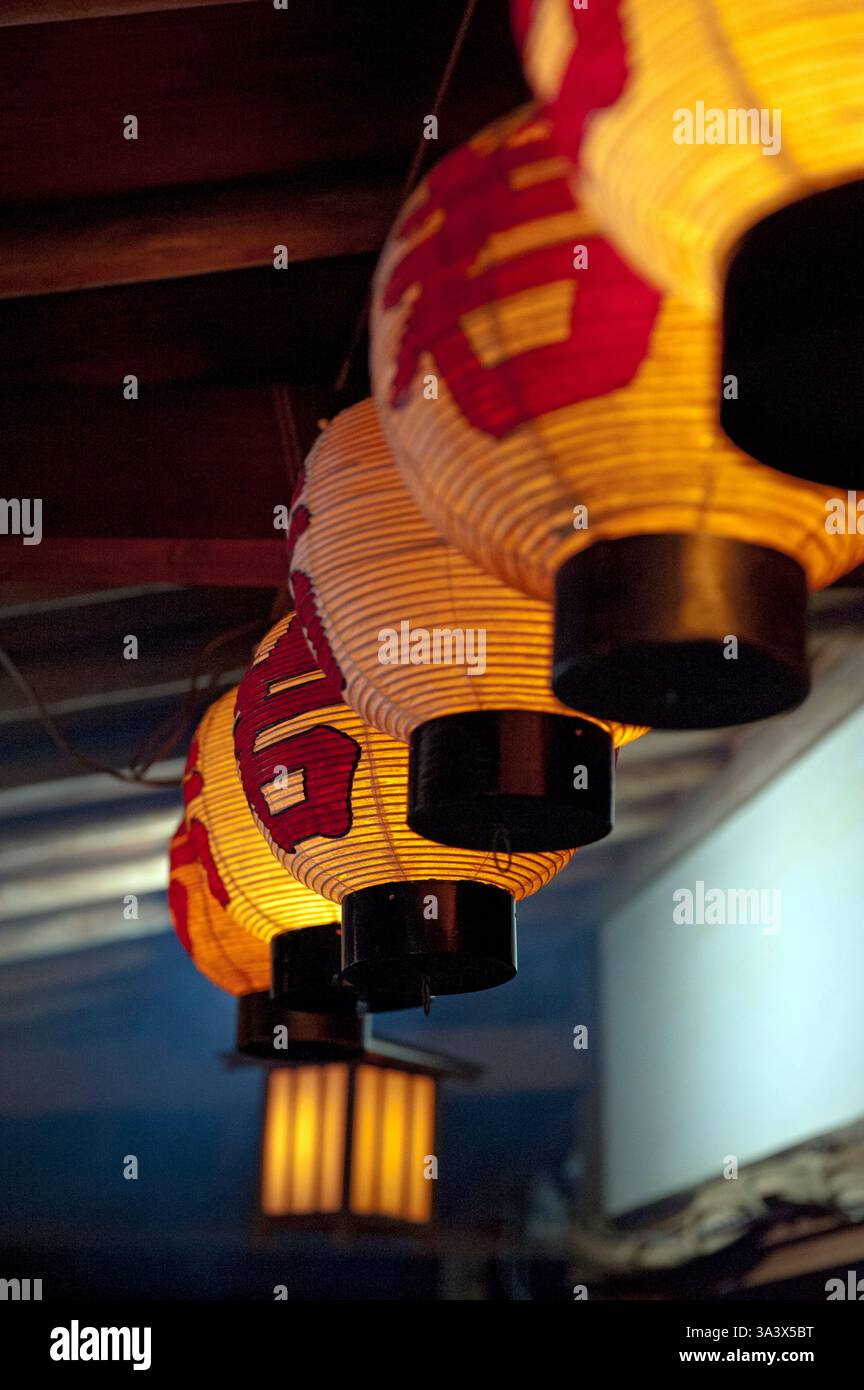 A row of warm glowing Japanese chochin paper lanterns hanging from the ...