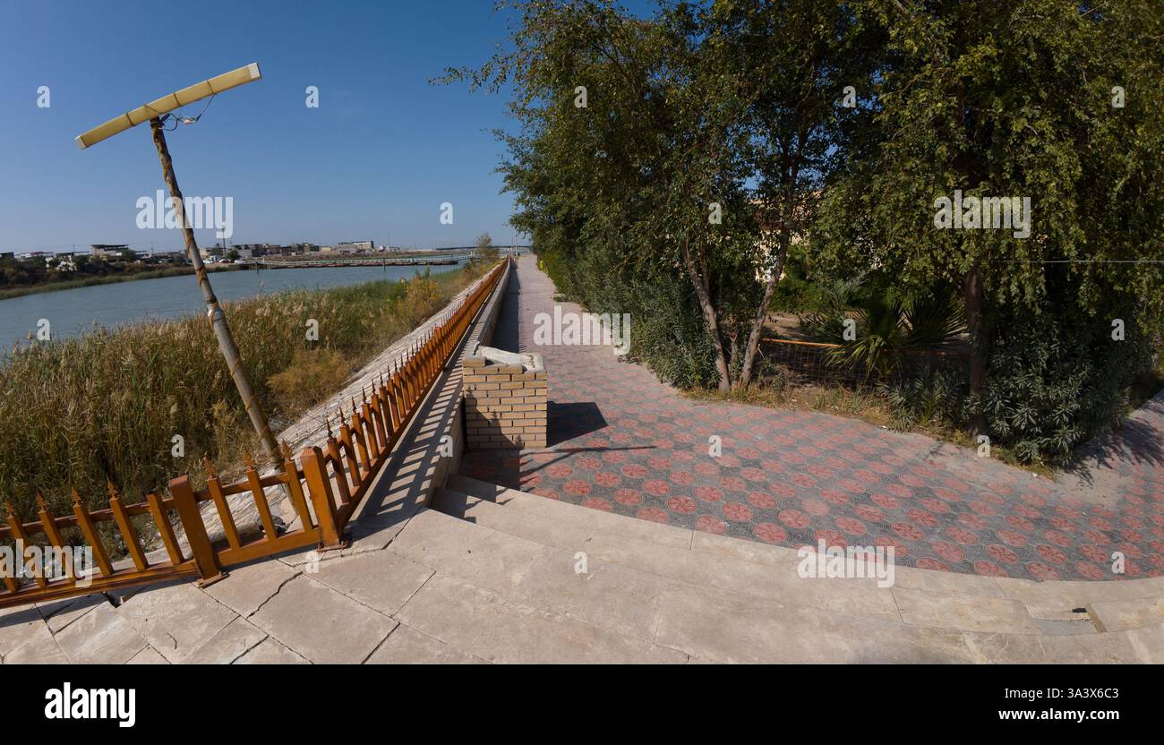 A scenic riverside walkway with a brick path, lined with trees and a ...