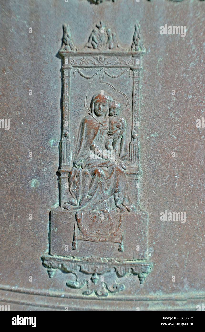 close-up of a weathered bronze carving on a bell, shows a seated Virgin ...