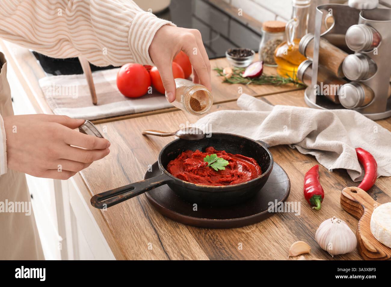 Young woman with bowl adding spices into tomato paste on table in ...