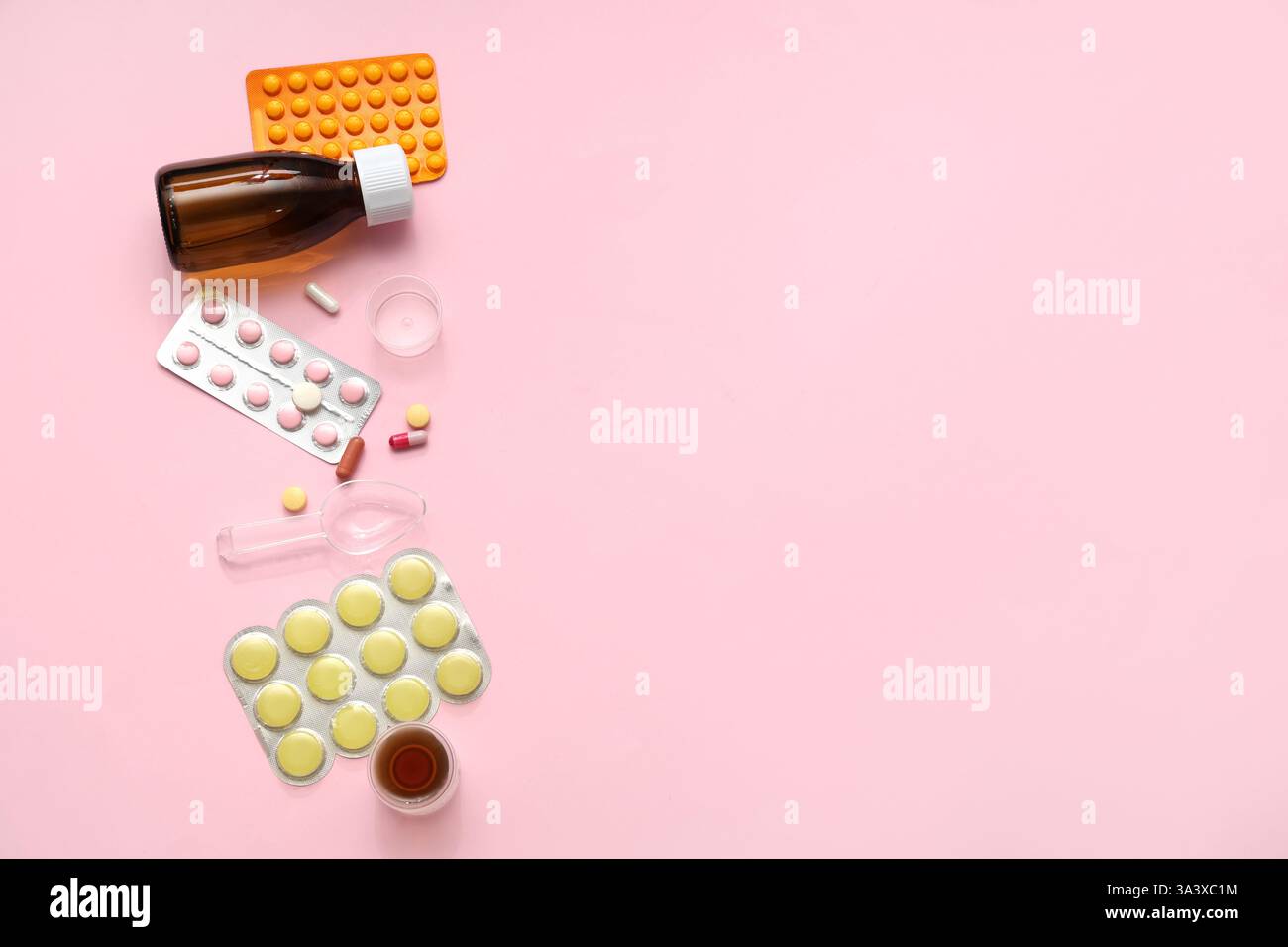 Bottle of cough syrup with measuring cups, spoon and different pills on ...