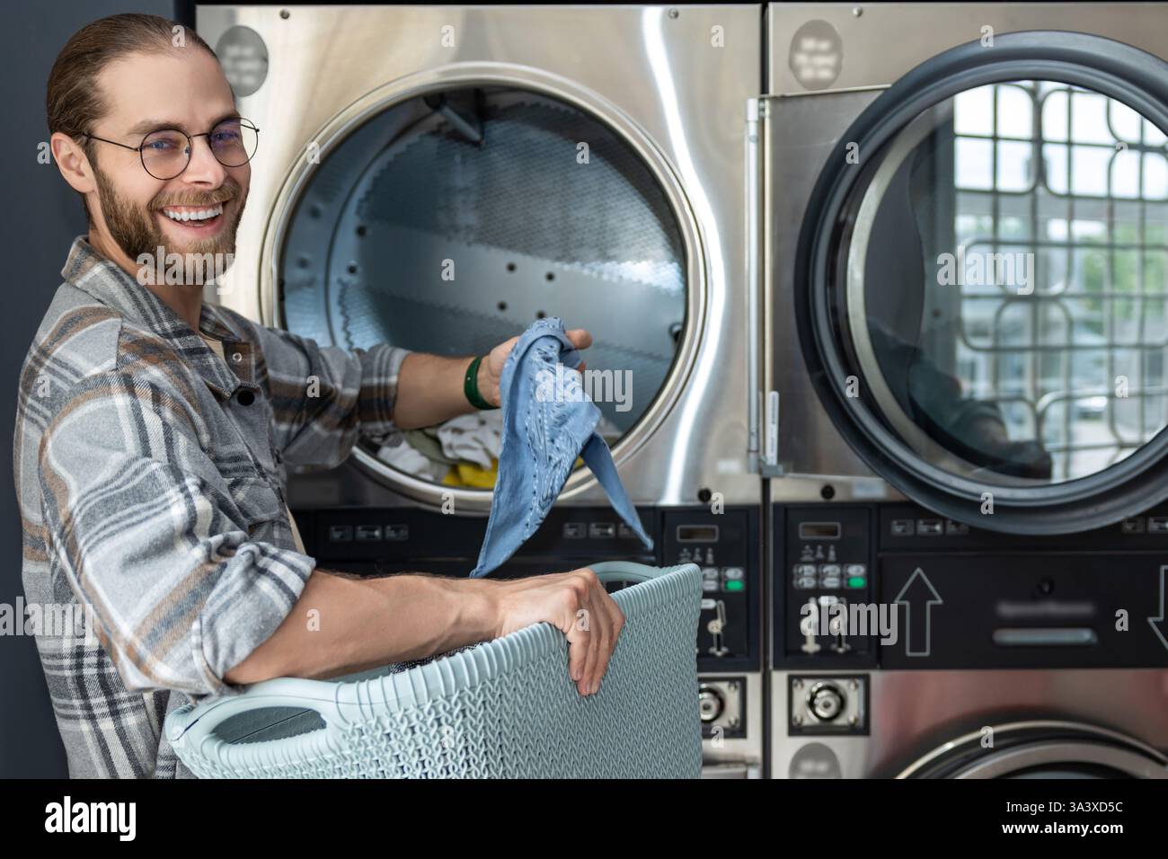 Man in public laundromat loading dirty clothes into washing machine ...