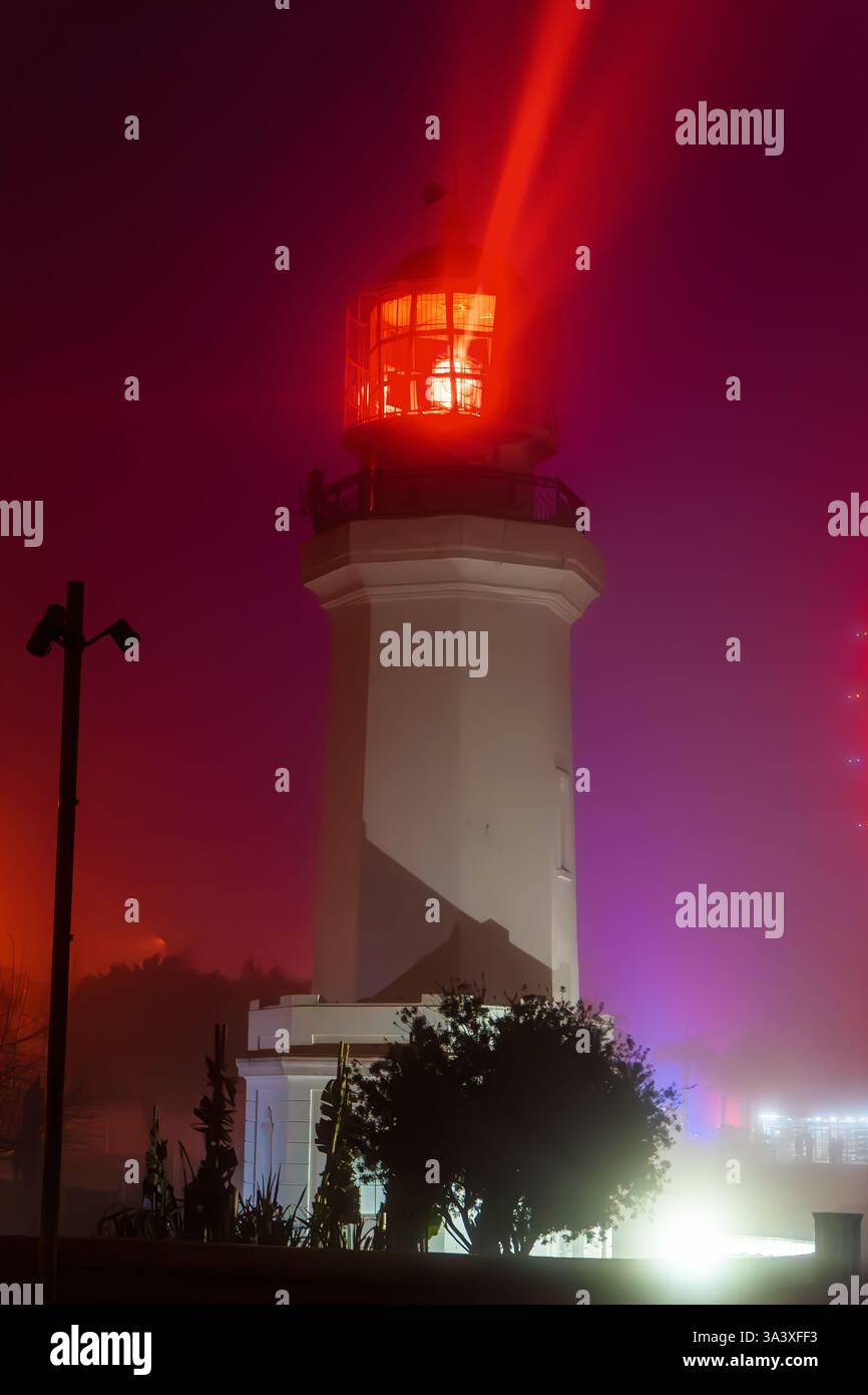 Lighthouse emitting powerful red beam through thick fog, dramatic and ...