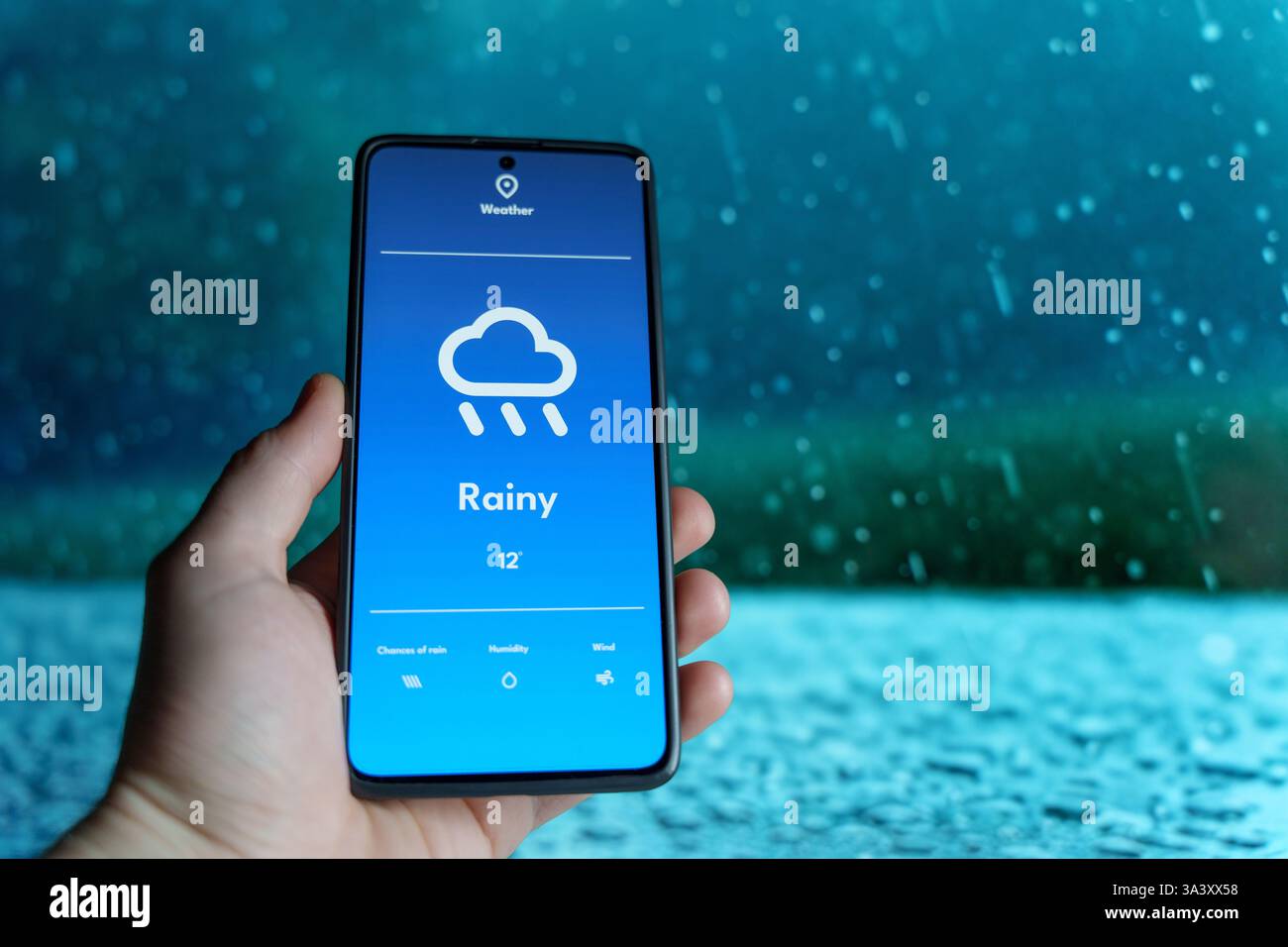 Hand holding a smartphone displaying a weather app with a rainy forecast. Raindrops falling in ...
