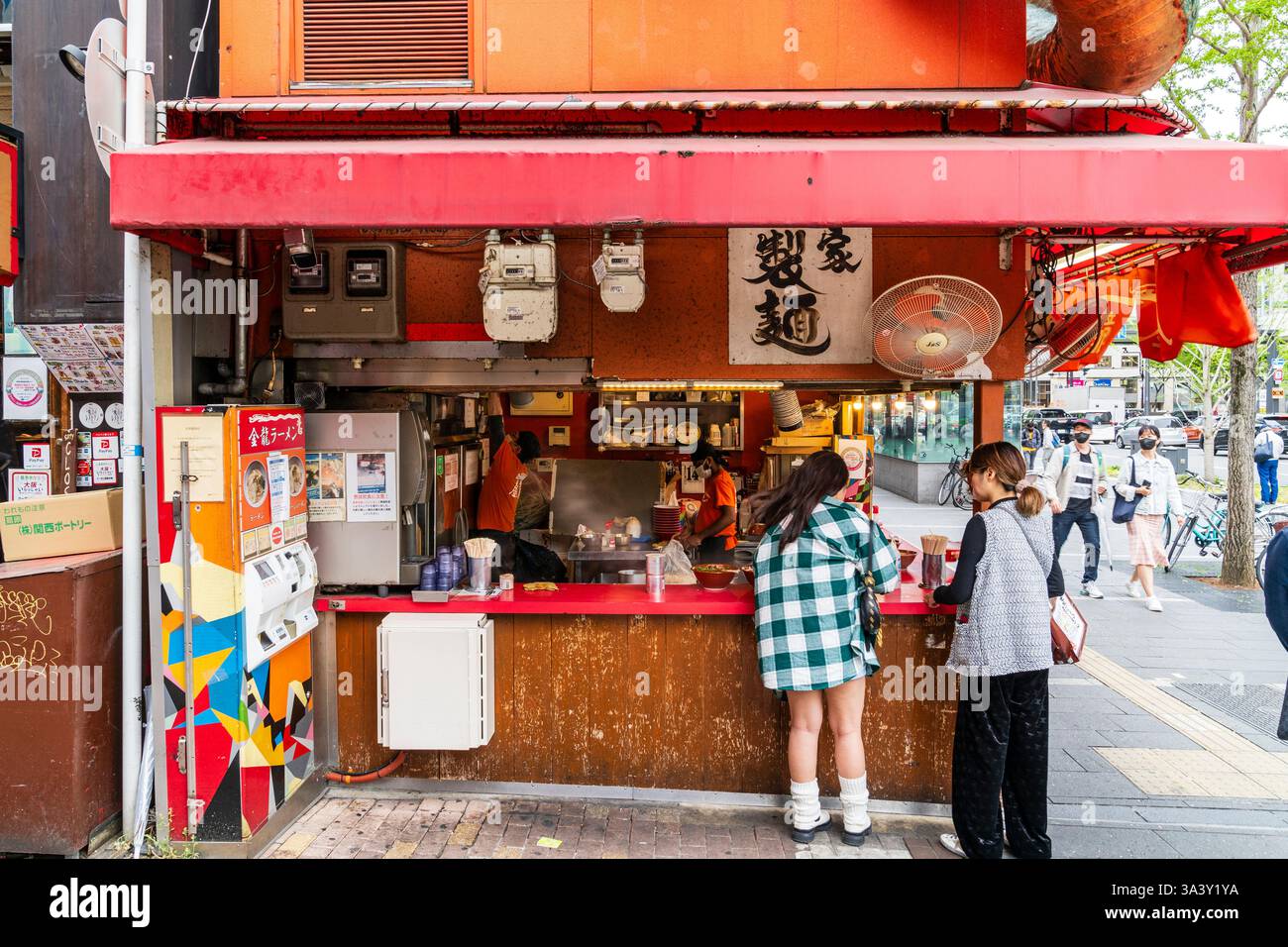 Two Japanese young women standing at the street counter of a branch of ...