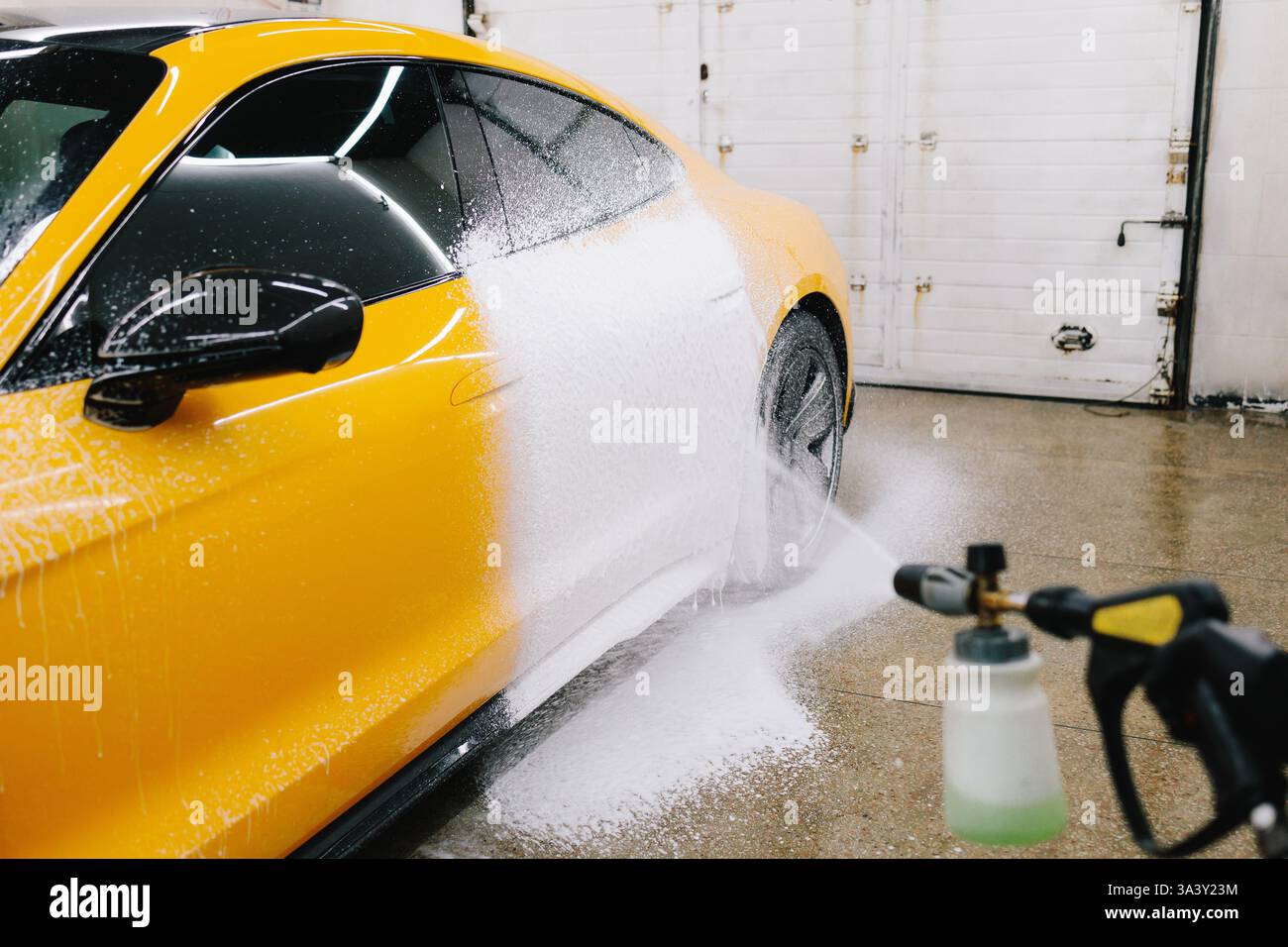 Worker sprays soap solution with high pressure water jet for detailing ...