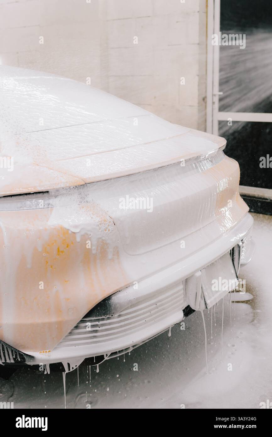 High-pressure water gun spraying soapy solution onto the vehicle's ...