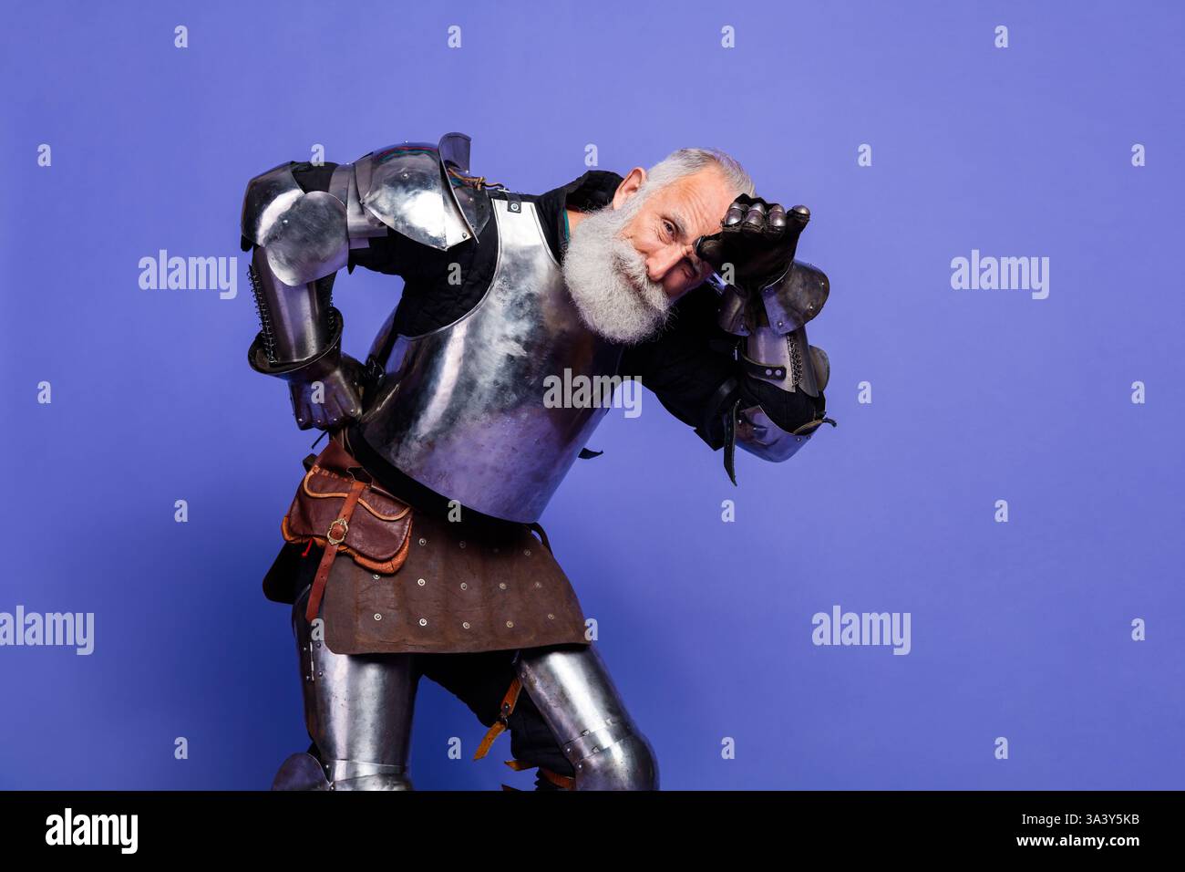 Mature bearded man in medieval knight armor posing against purple ...