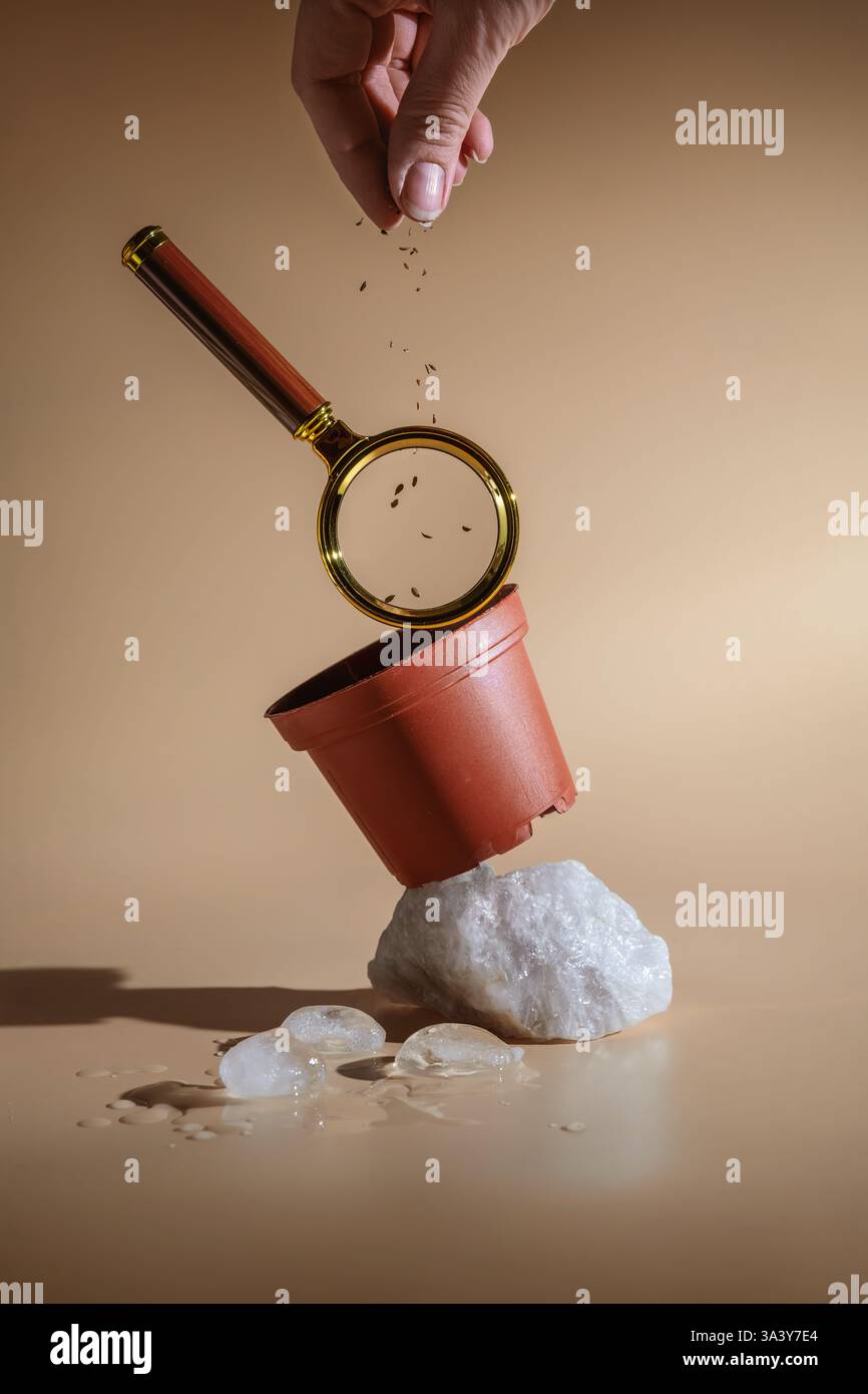 Hand is dropping seeds through a magnifying glass over a terracotta ...