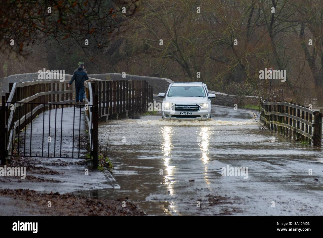 A white Ford pick-up driving towards the viewer pushing a small wave ...