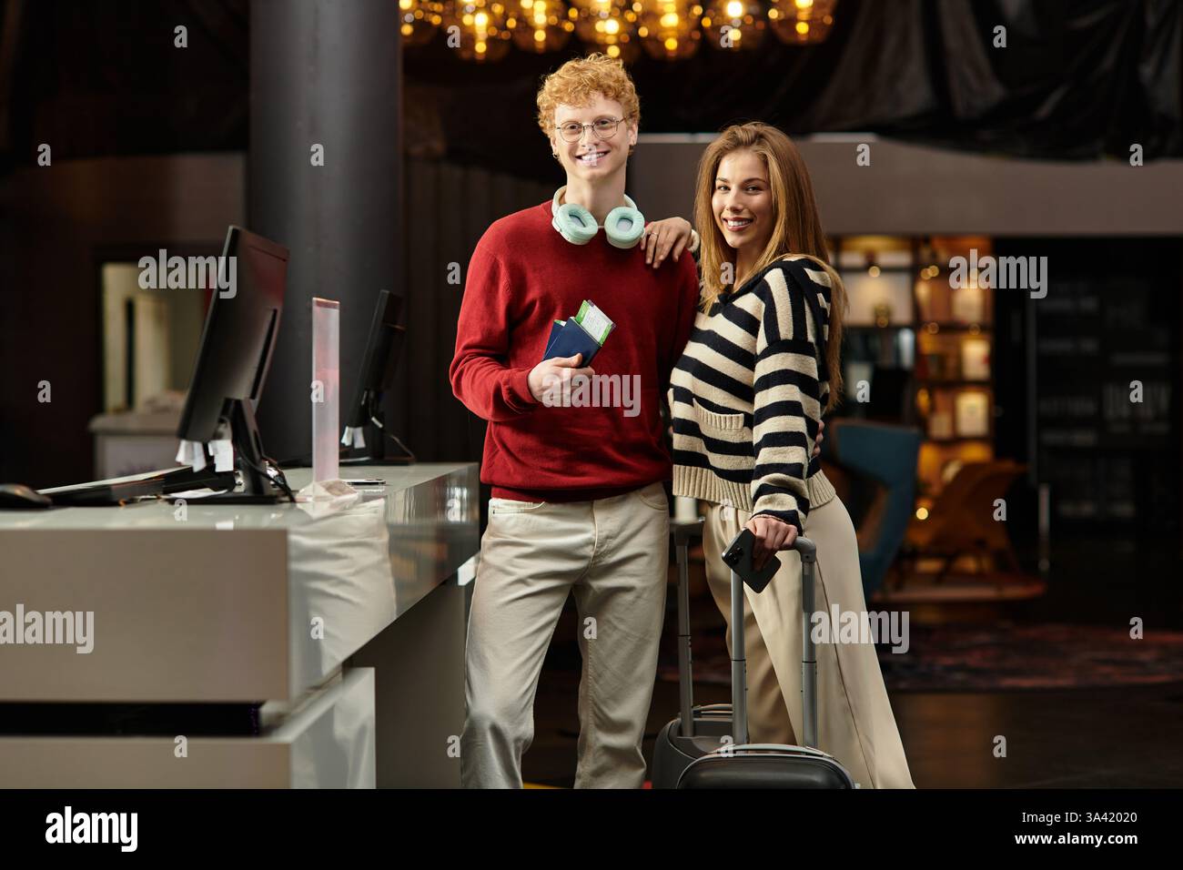 A young couple stands at a hotel reception, sharing a moment filled ...
