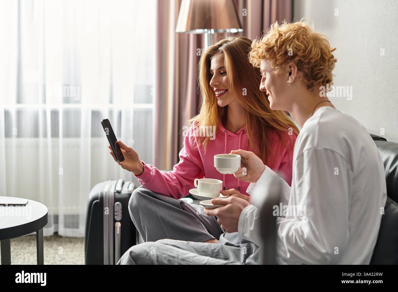 A loving couple smiles at their phone while sharing cups of coffee in a ...