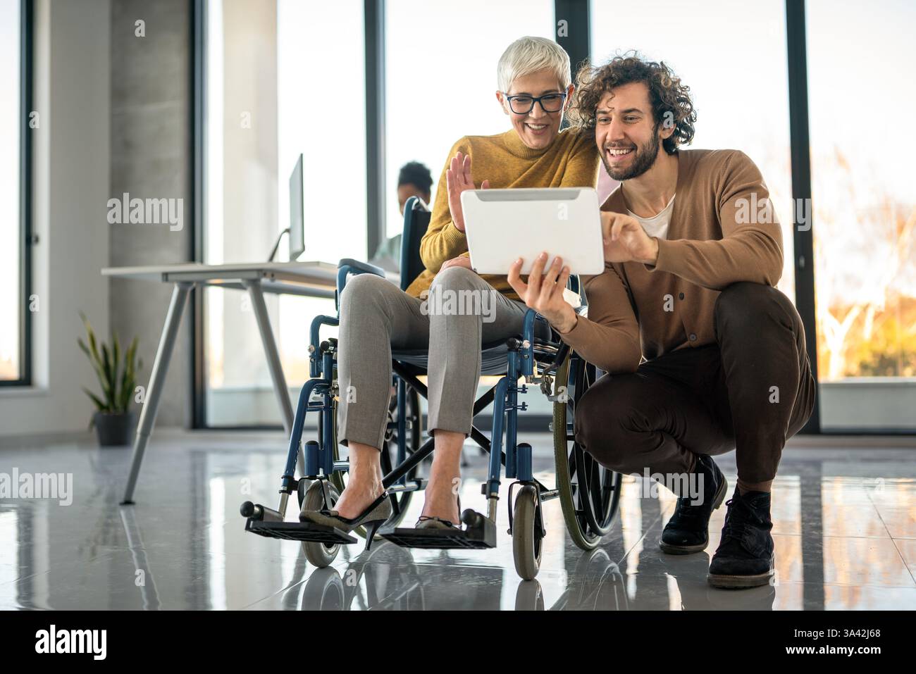 Business woman in wheelchair working with colleague in modern inclusive ...