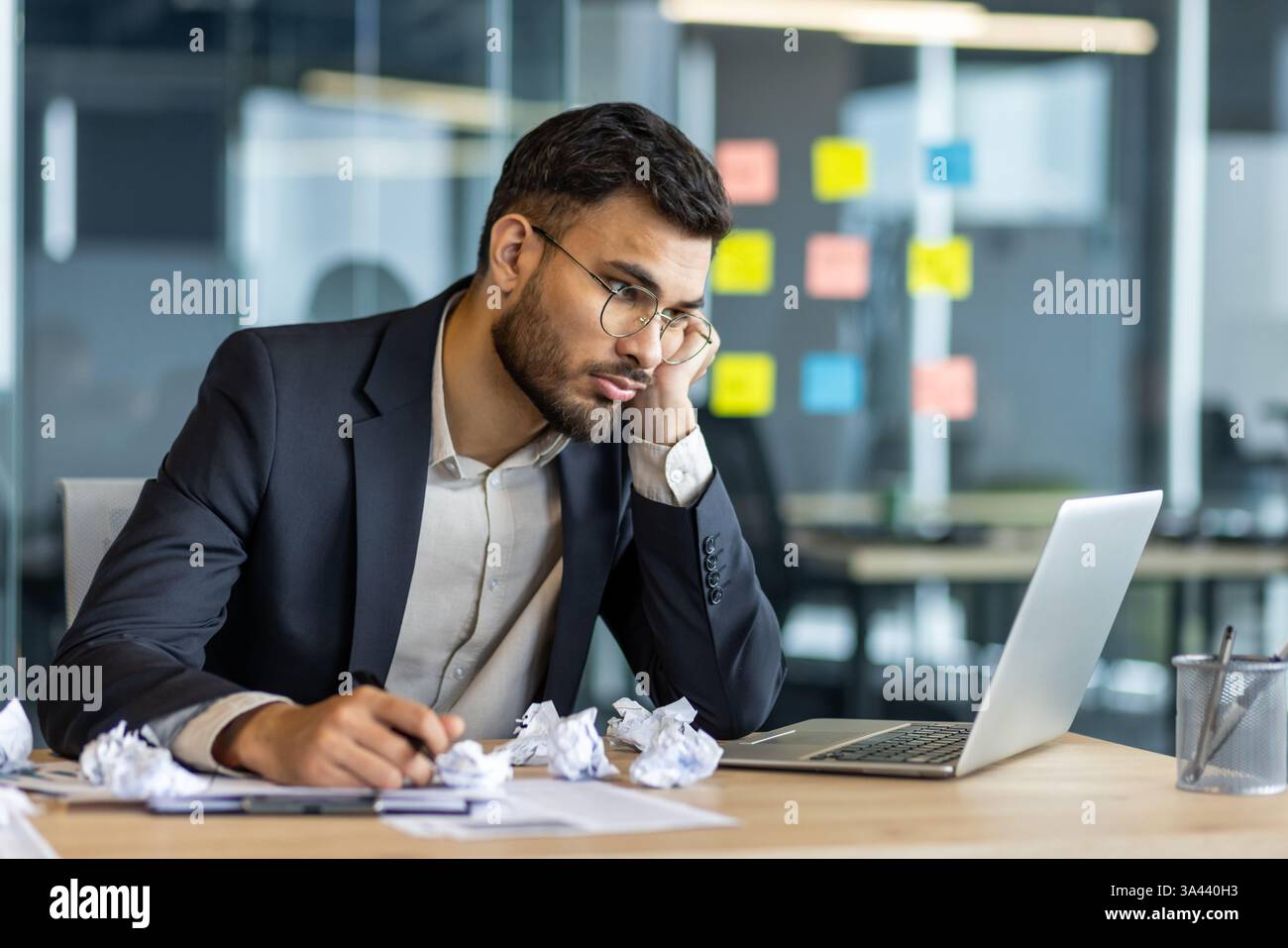 A pensive financier sits at his desk surrounded by crumpled paper ...