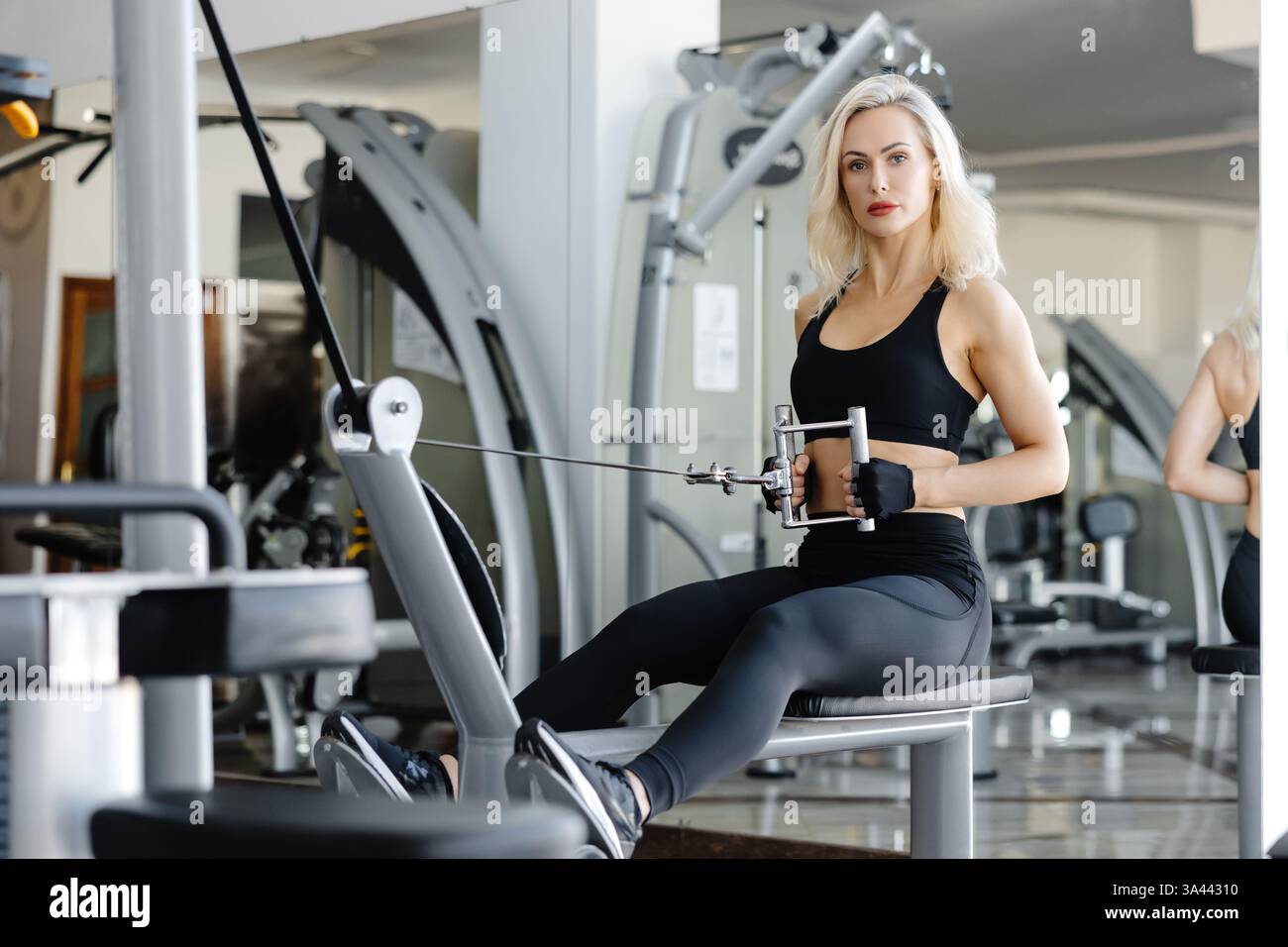 Strong female athlete exercising back muscles using cable row machine ...