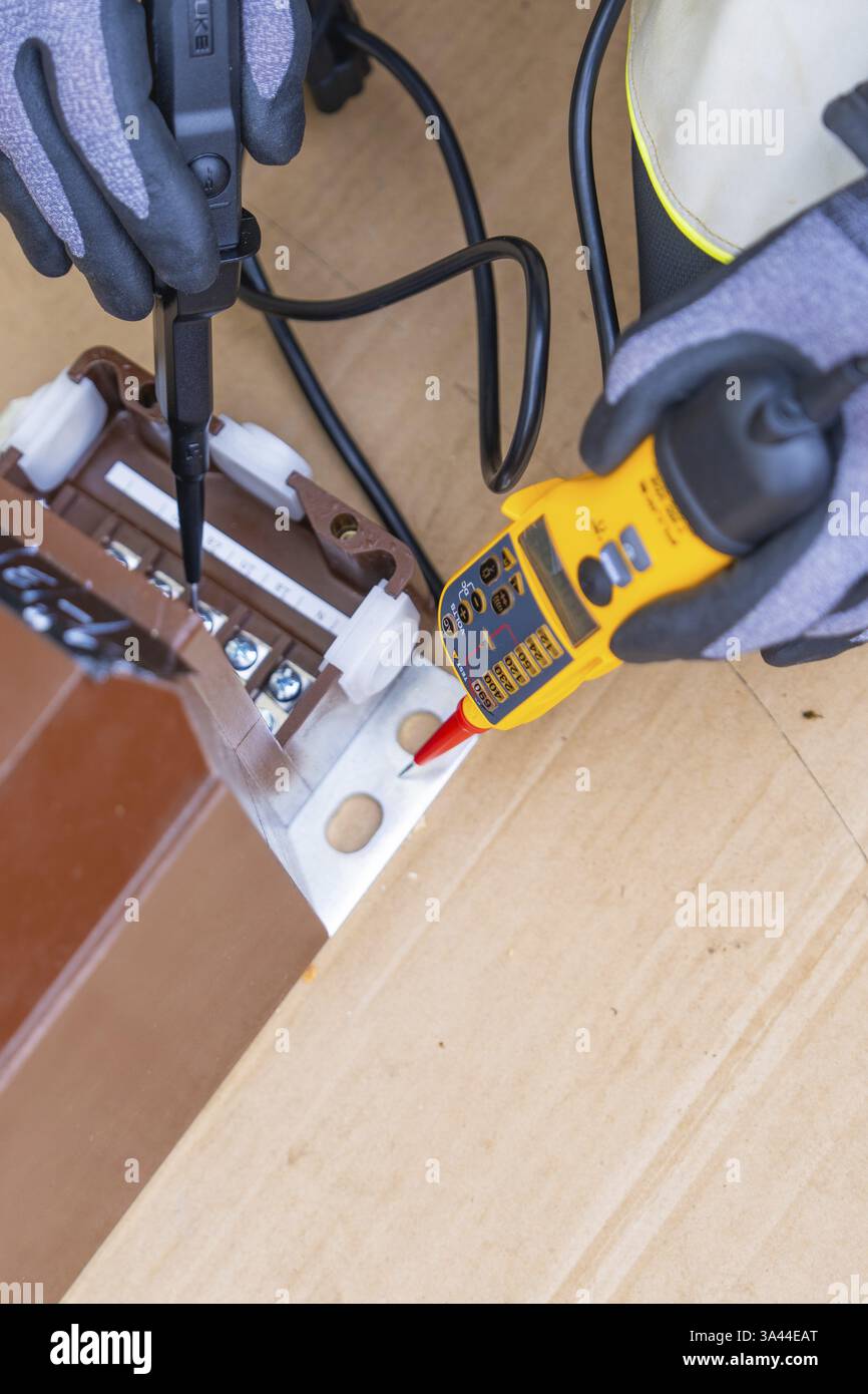 Close-up of two hands examining an electrical component with a tester ...