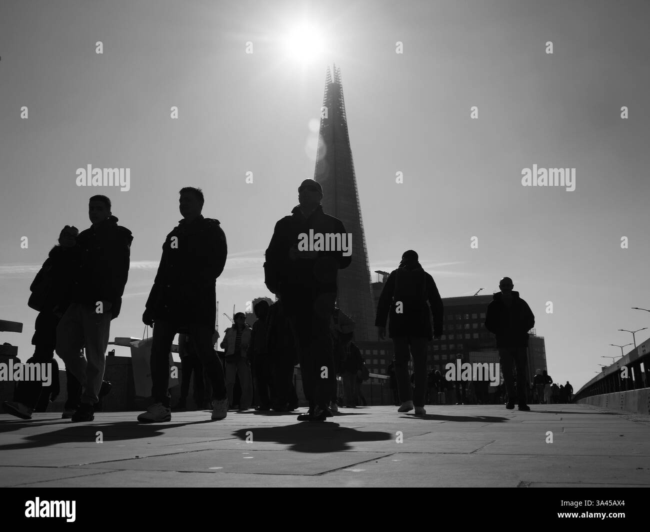 Commuters walking over London Bridge in bright winter sunlight, with ...