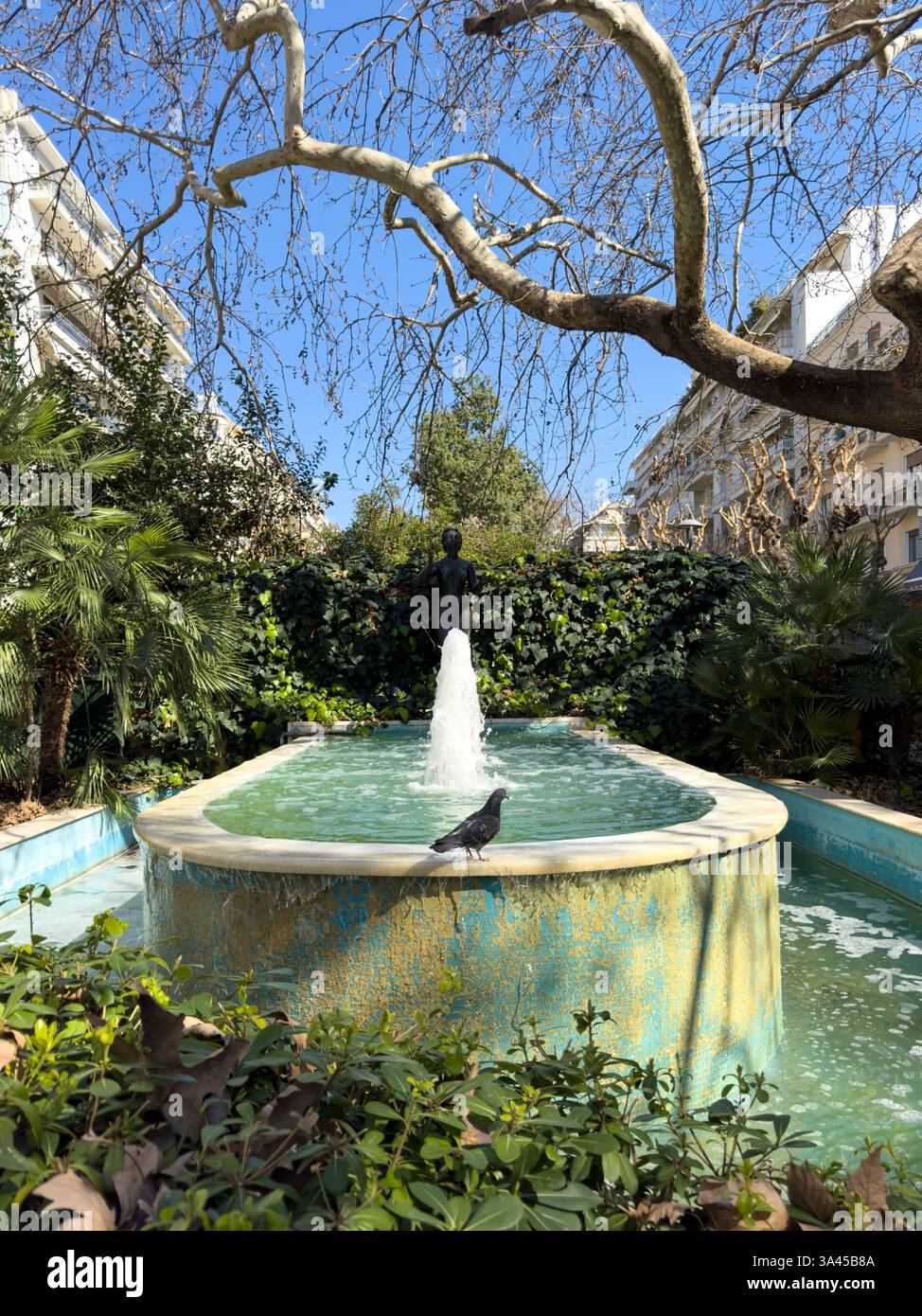 A fountain in a local tranquil Greek park, adorned by a pigeon, offers ...