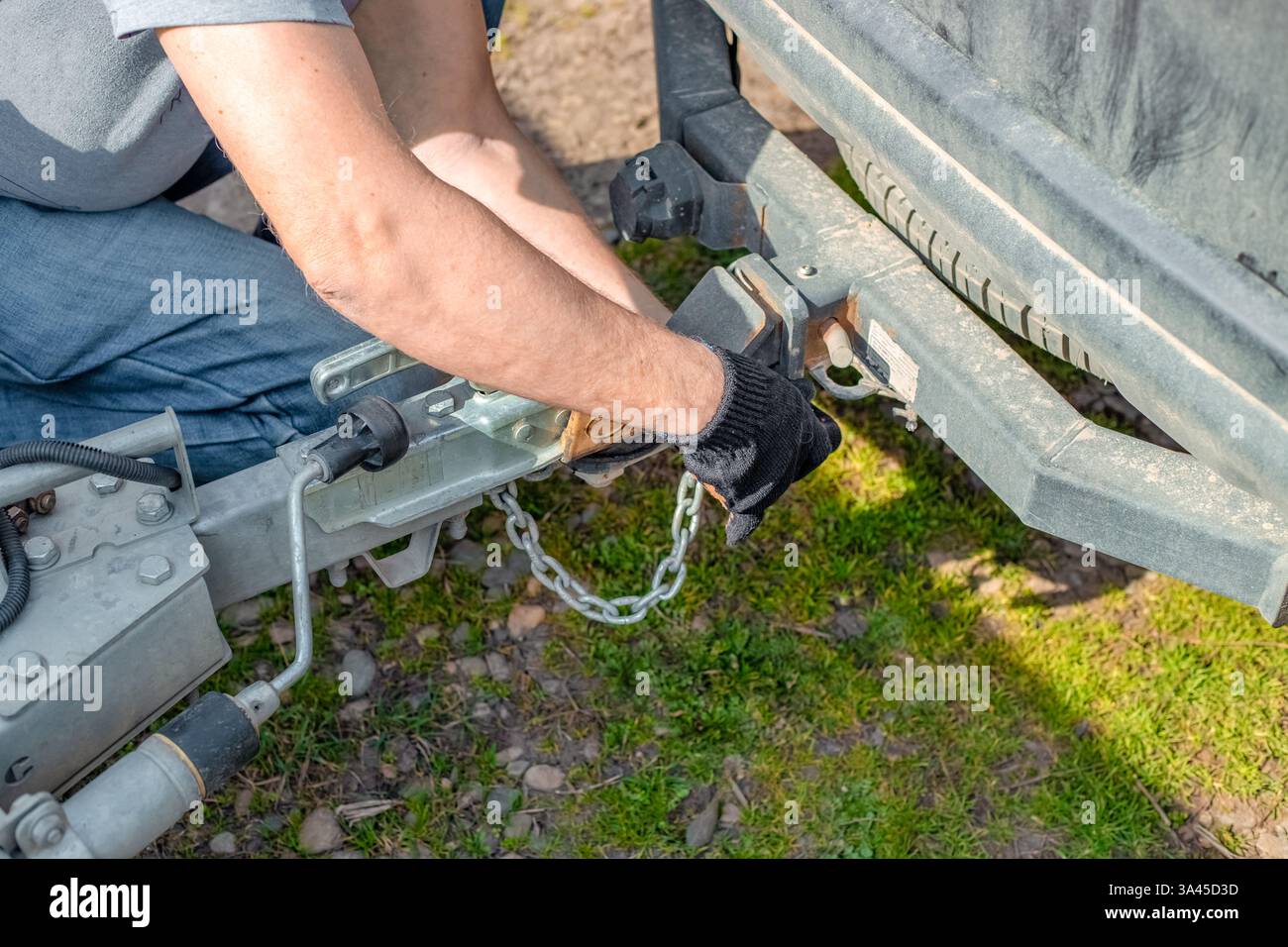 A man attaches a trailer to a car, securing safety chains to the ...