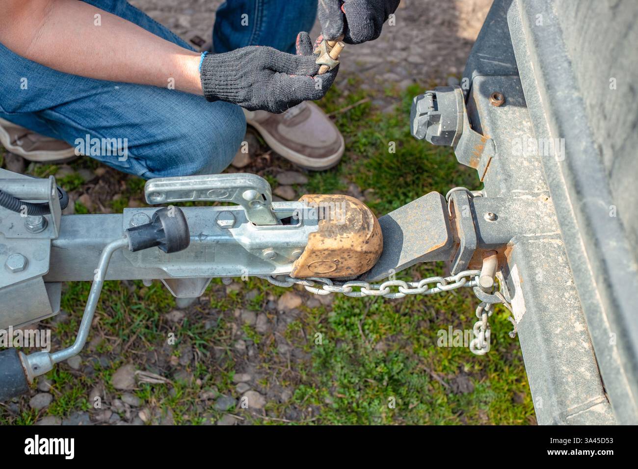 A man attaches a trailer to a car, securing safety chains to the ...