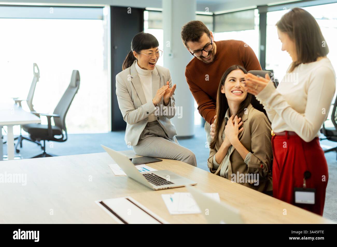 In a contemporary workspace, colleagues share smiles and applause ...