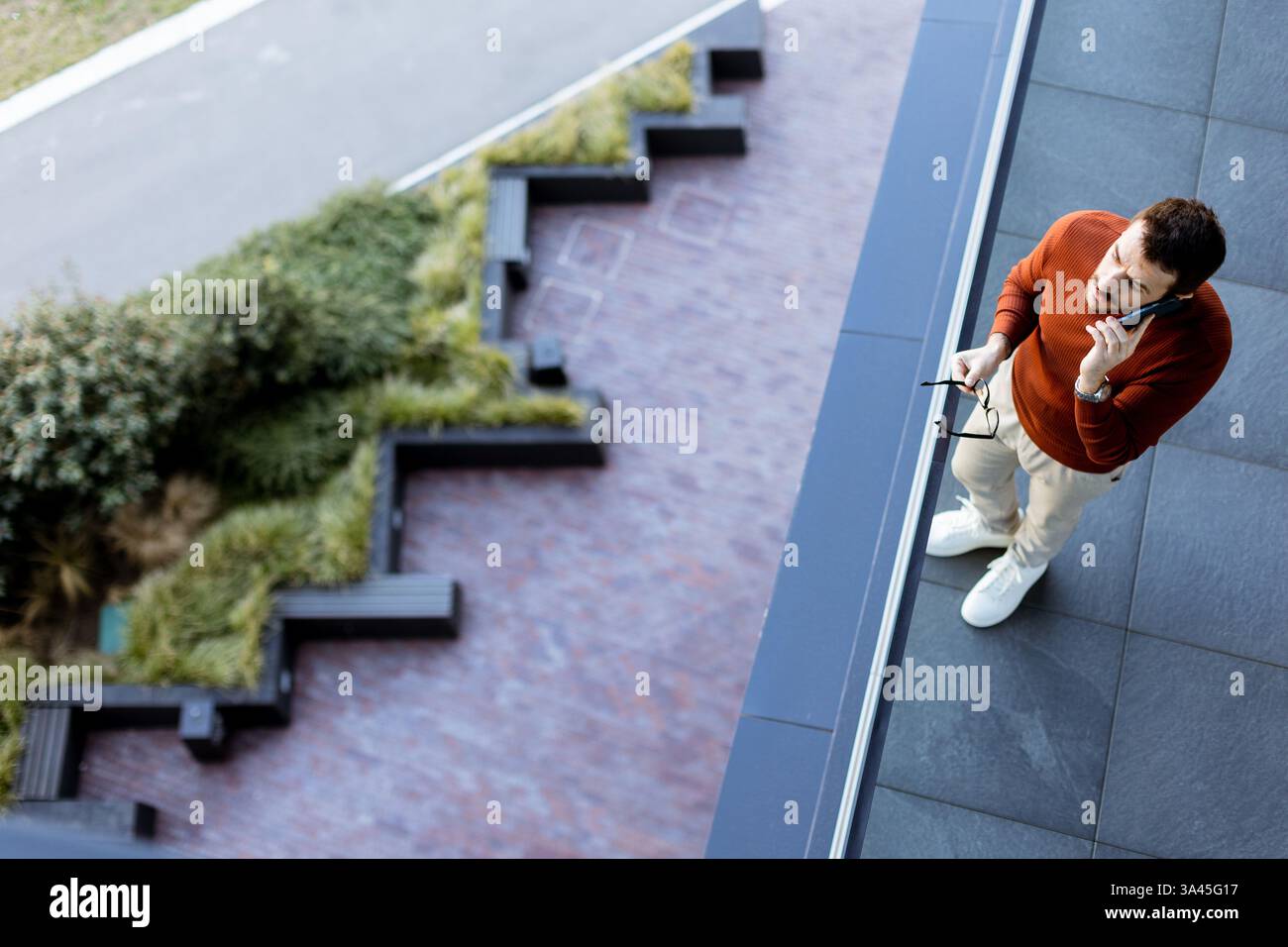 A young man stands on a sleek balcony while engaged in an animated ...