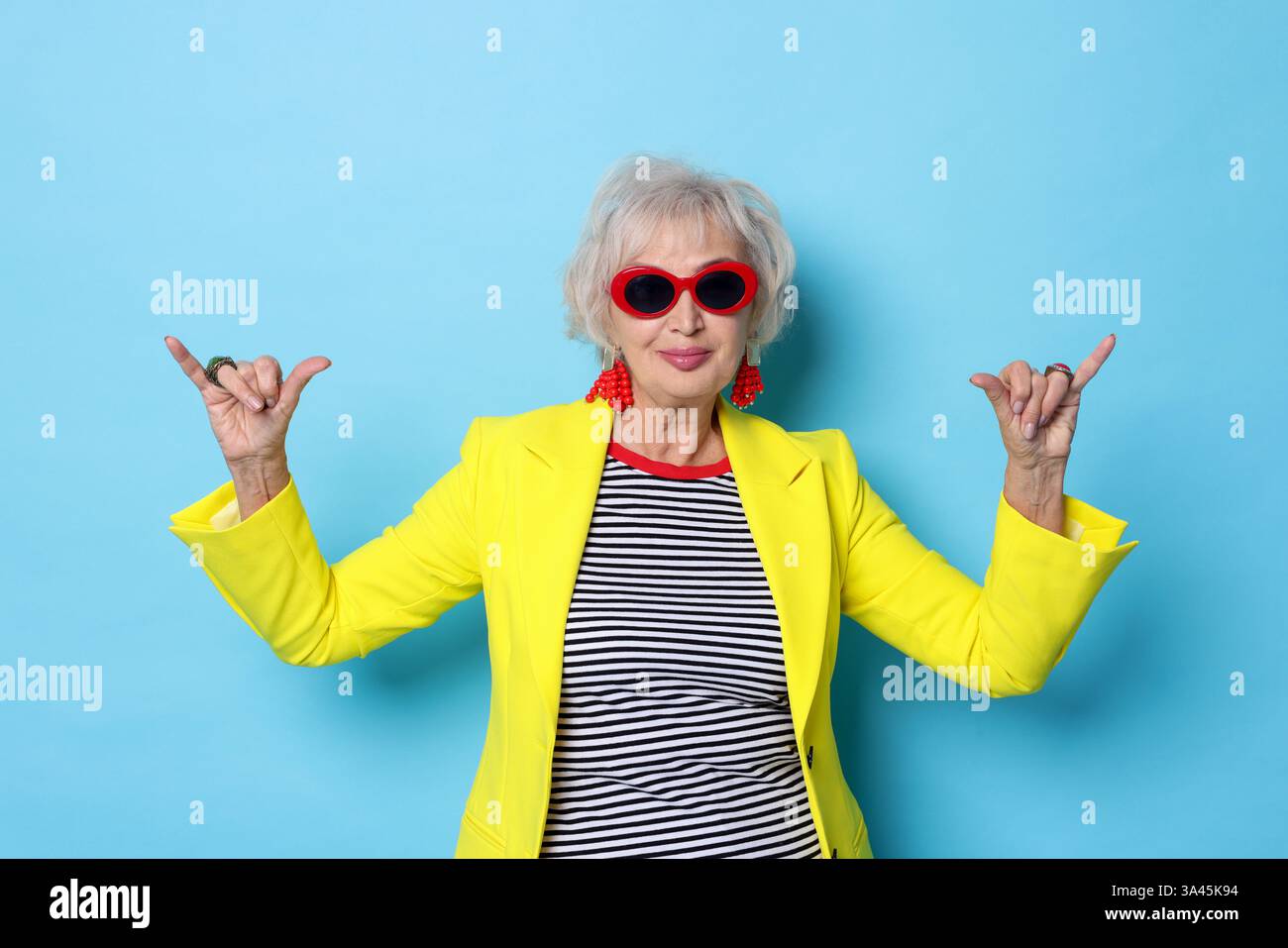 Cool grandmother in sunglasses showing shaka gesture on light blue ...