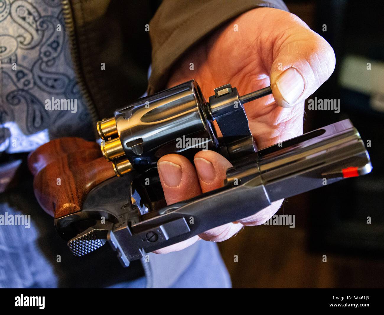 A man ejects spent casings from a black revolver by pushing on the ...