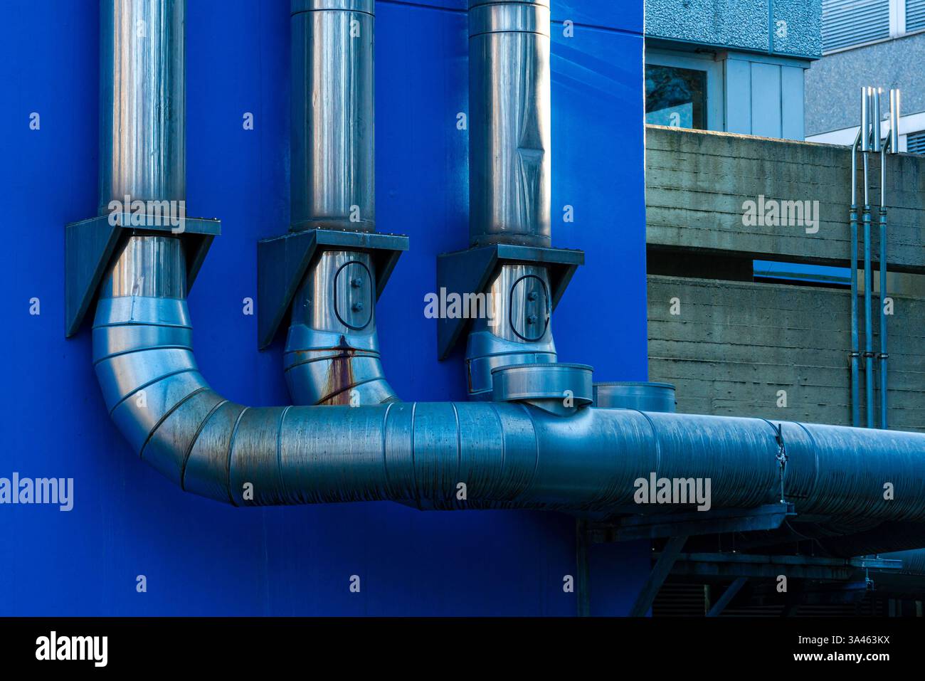 Metallic pipes run along a vibrant blue wall in an urban setting ...